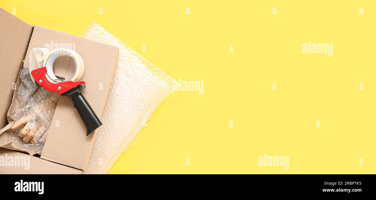 Packing tape dispenser, cardboard box, parcel and bubble wrap on yellow ...