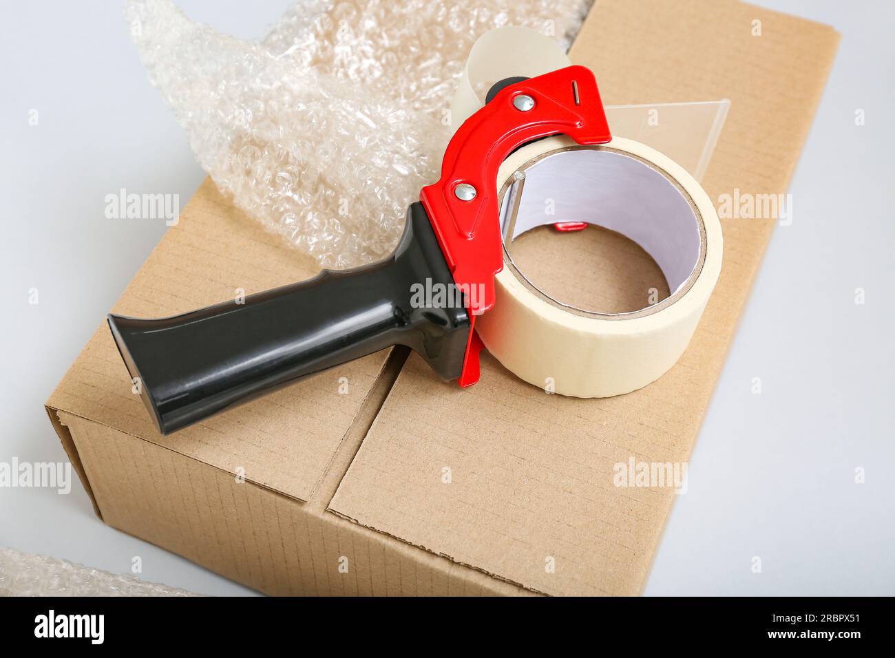 Packing tape dispenser, cardboard box and roll of bubble wrap on grey ...