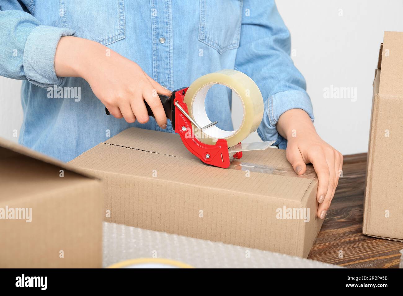 Woman packing cardboard box with adhesive tape dispenser at wooden ...