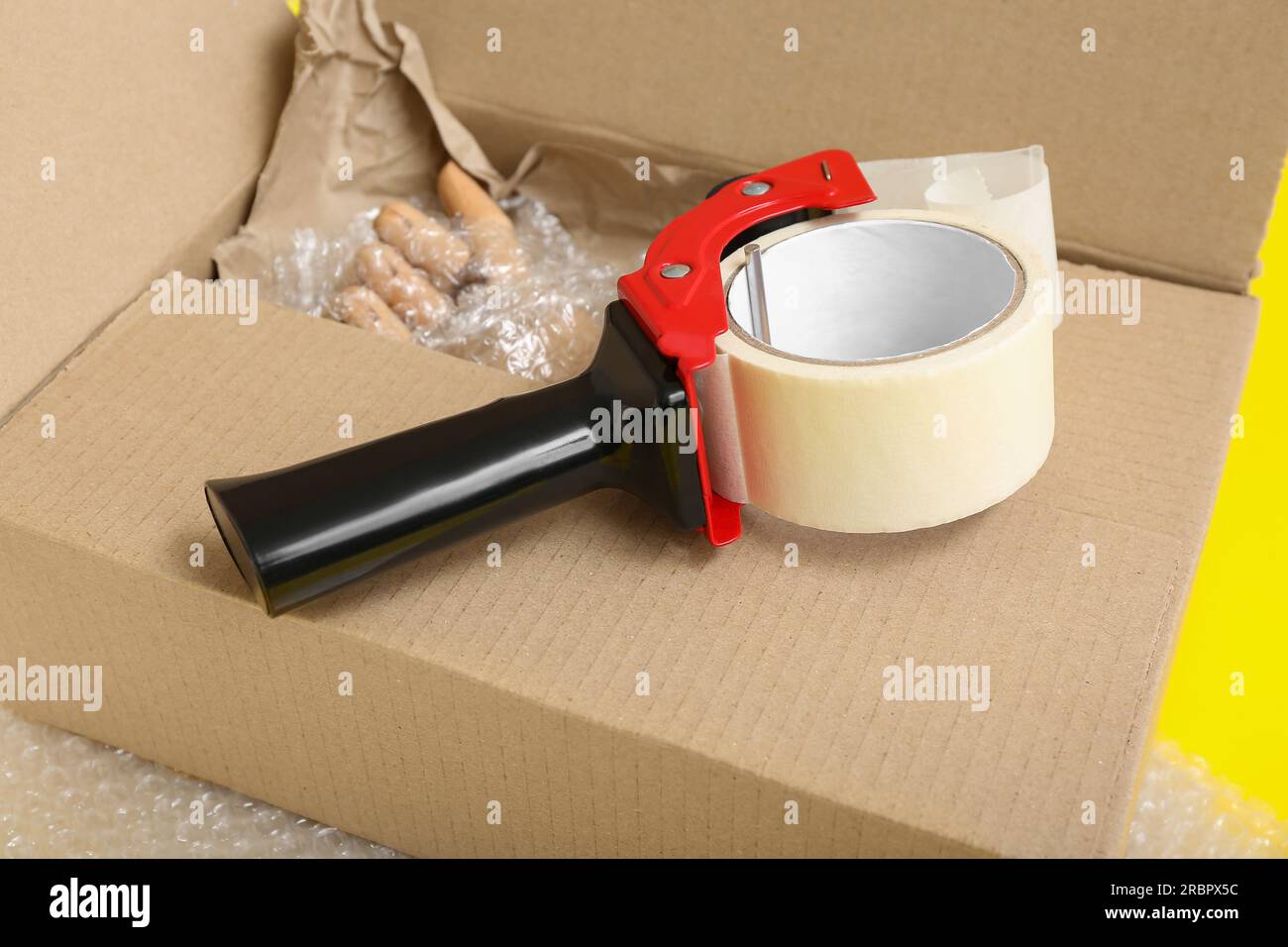 Packing tape dispenser and cardboard box on yellow background Stock ...
