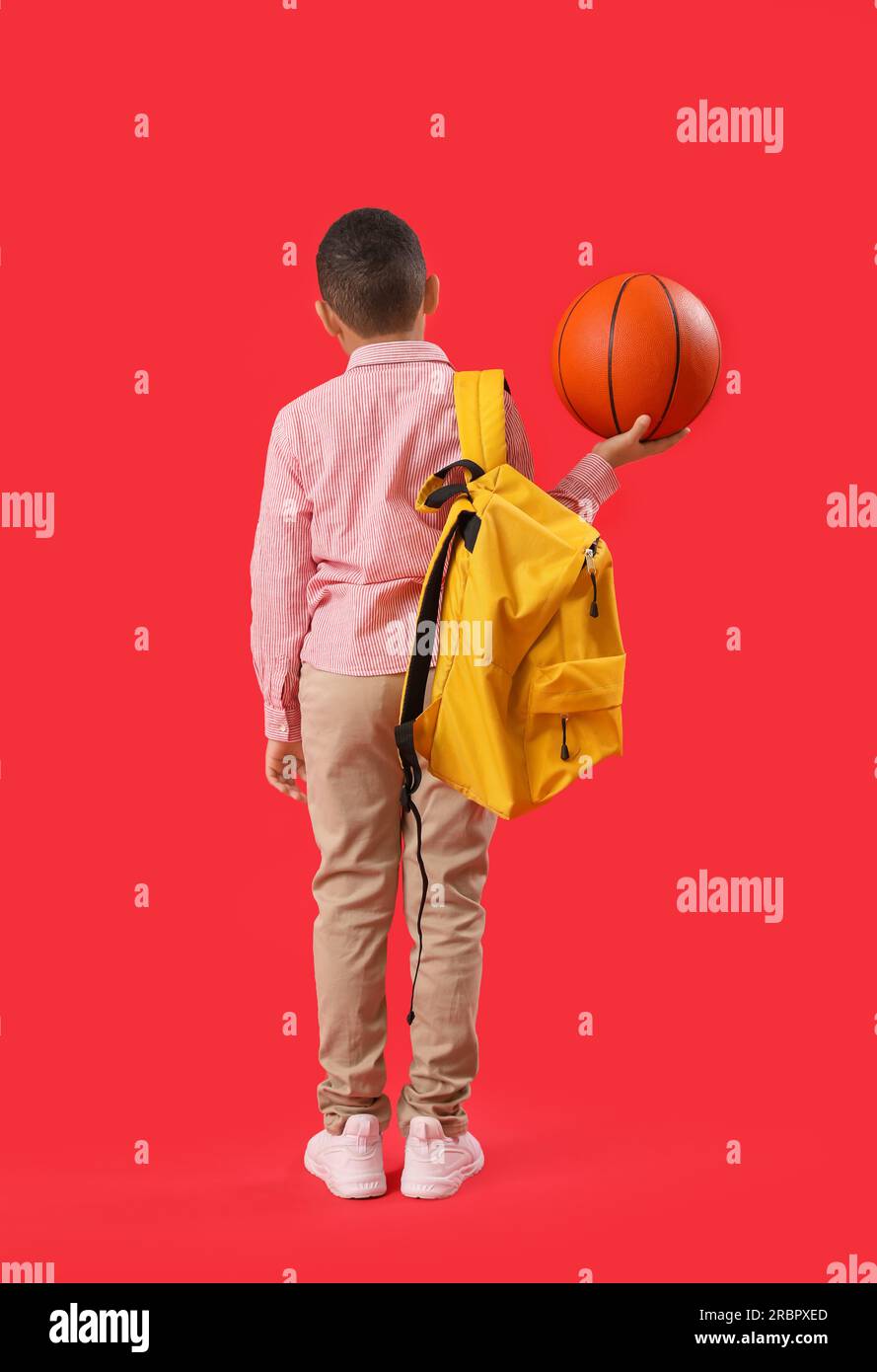 Little African-American schoolboy with ball and backpack on red ...
