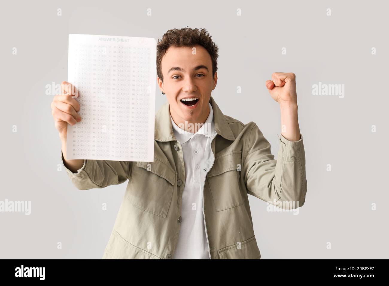 Happy male student with answer sheet for school test on grey background ...