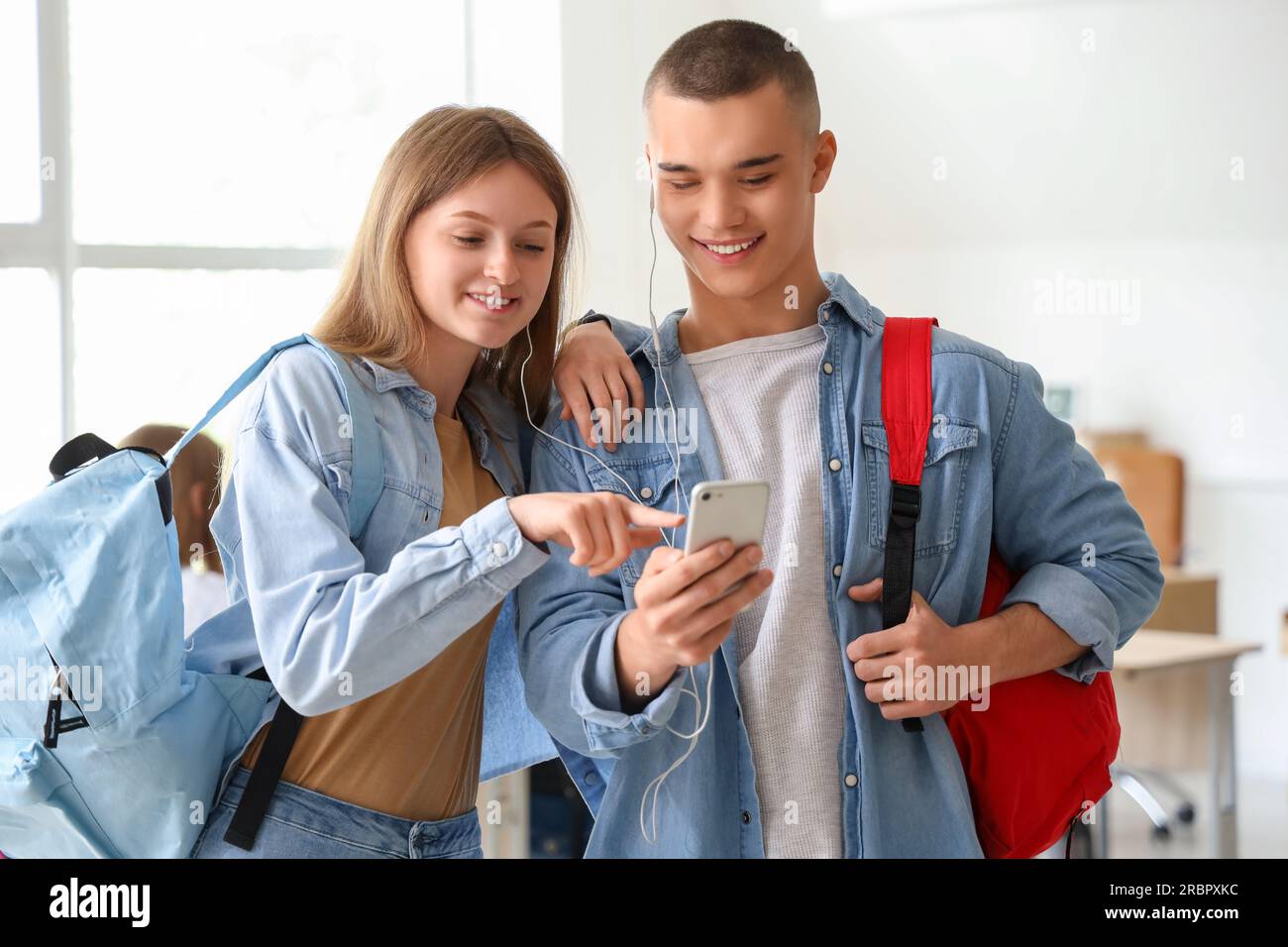 Happy students with backpacks using mobile phone in classroom Stock ...