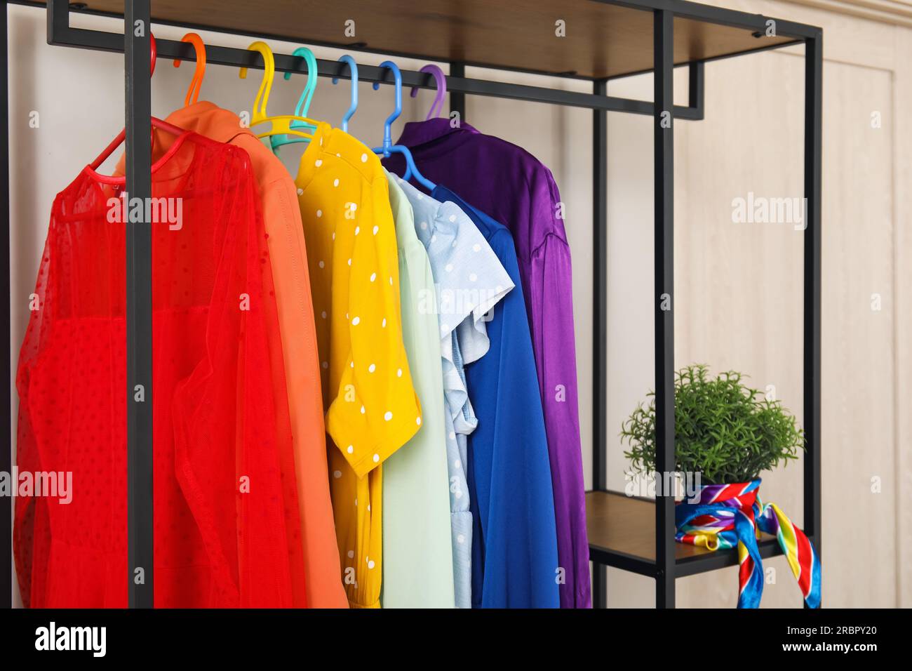 Shelving unit with colorful clothes and houseplant near white wall ...