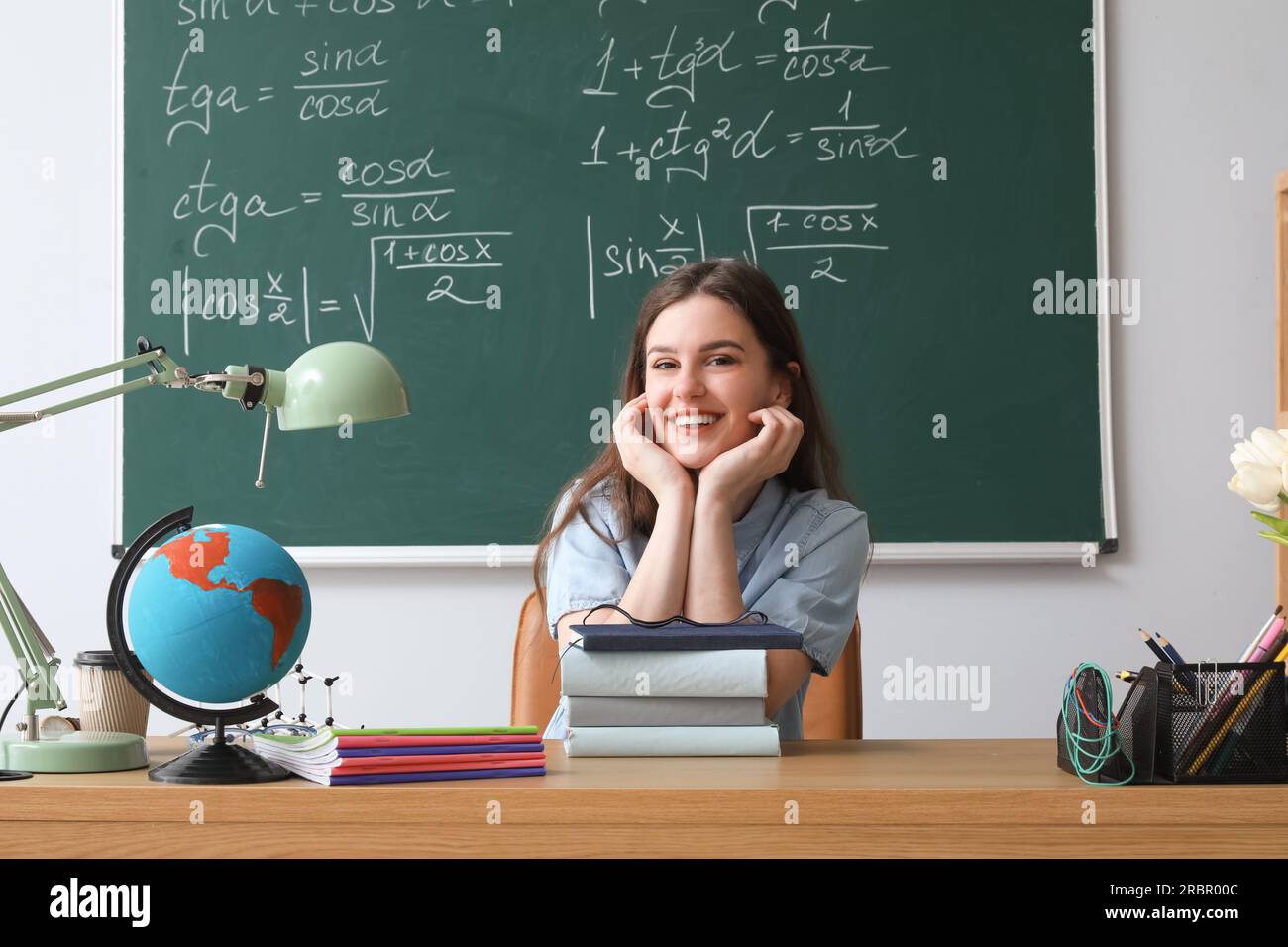Female teacher sitting at table in classroom Stock Photo - Alamy