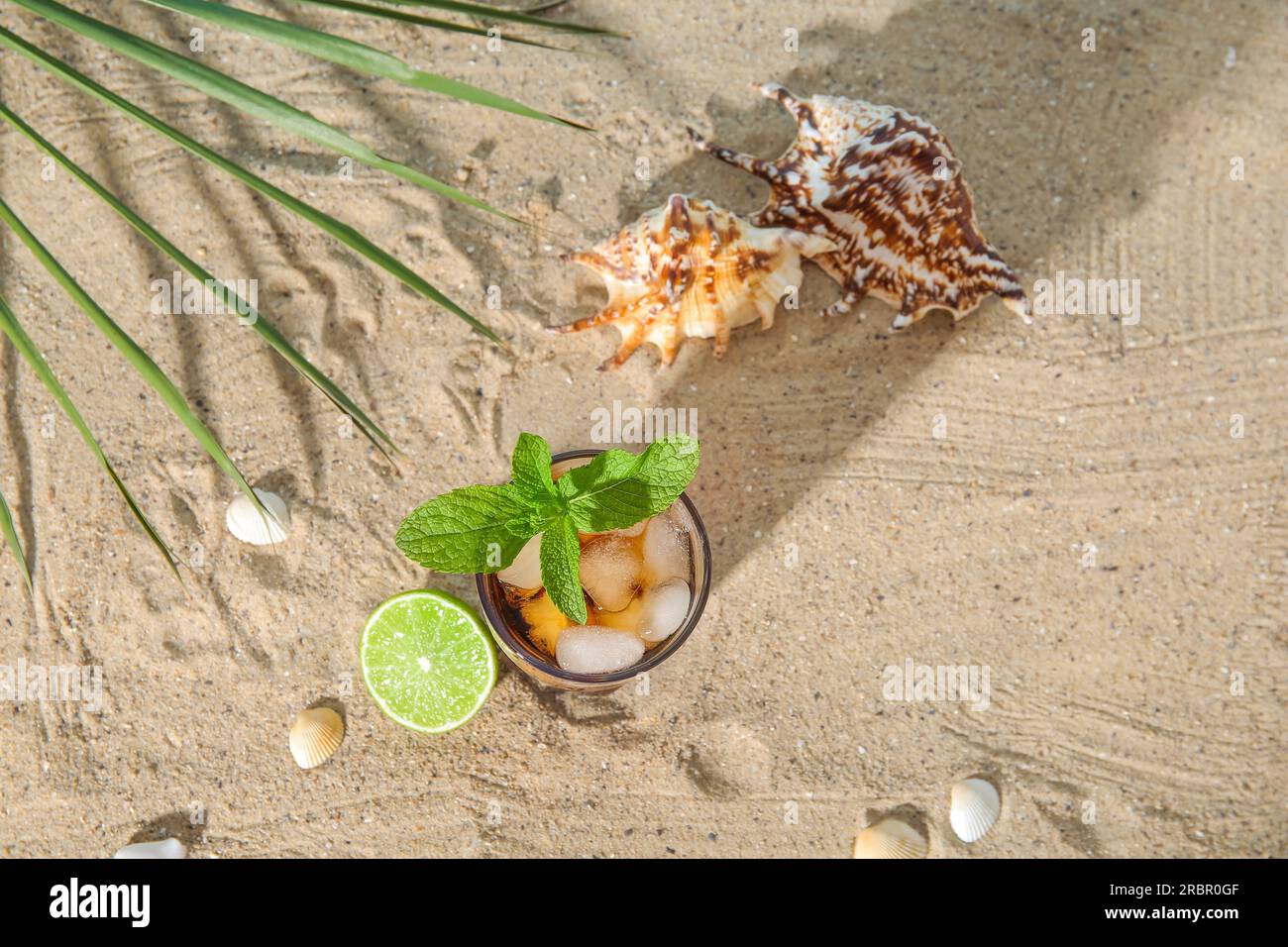 Glass of cold Cuba Libre cocktail and seashells on sand Stock Photo - Alamy