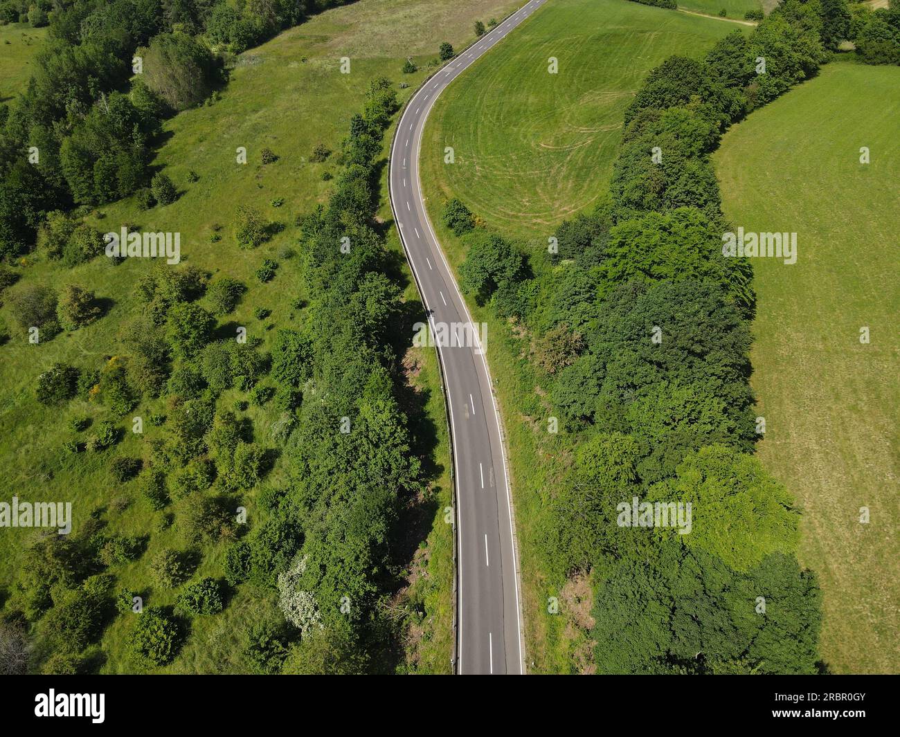 Drone view of a rural road with white stripes between trees and grass ...