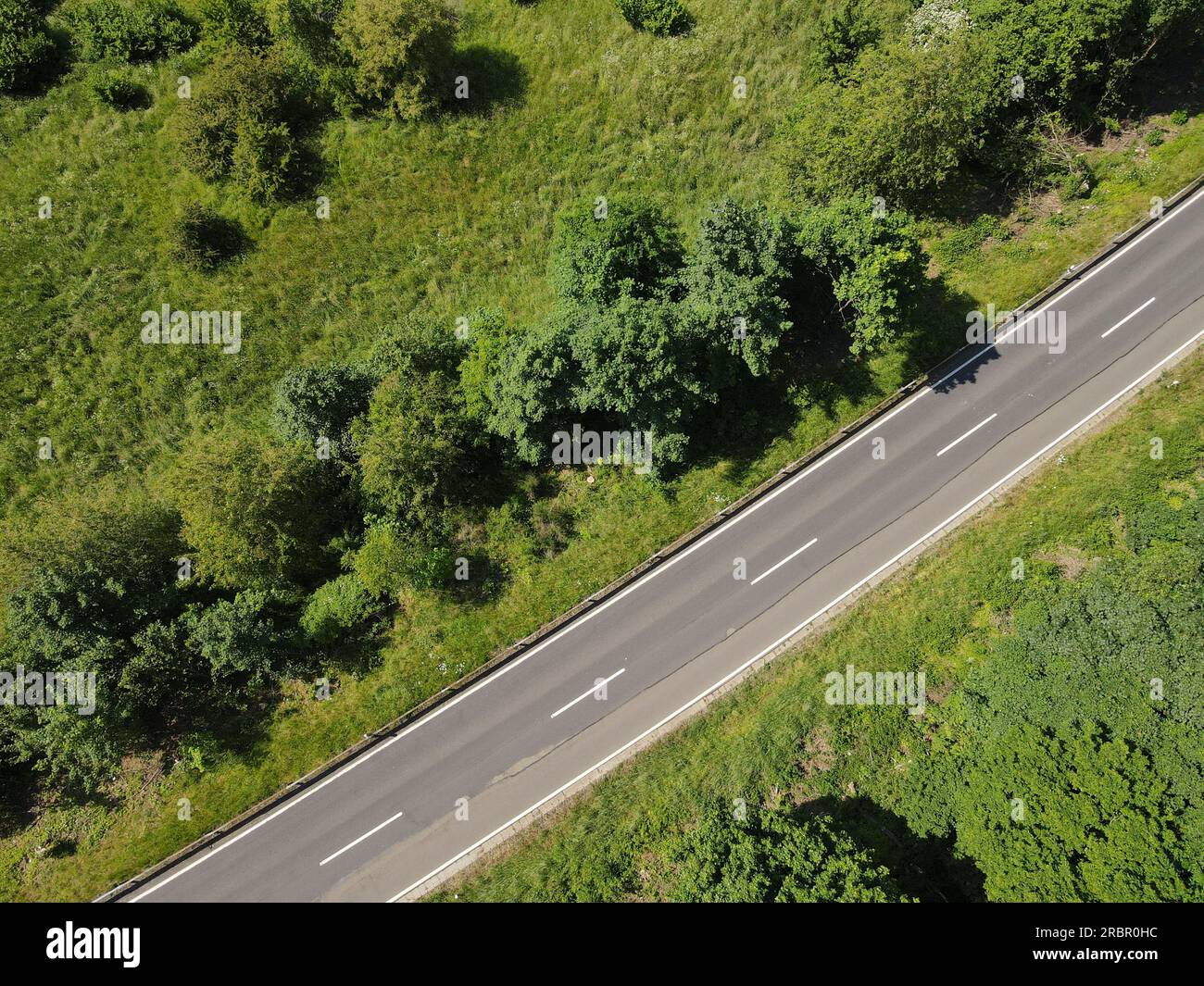 Drone view of a rural road with white stripes between trees and grass ...
