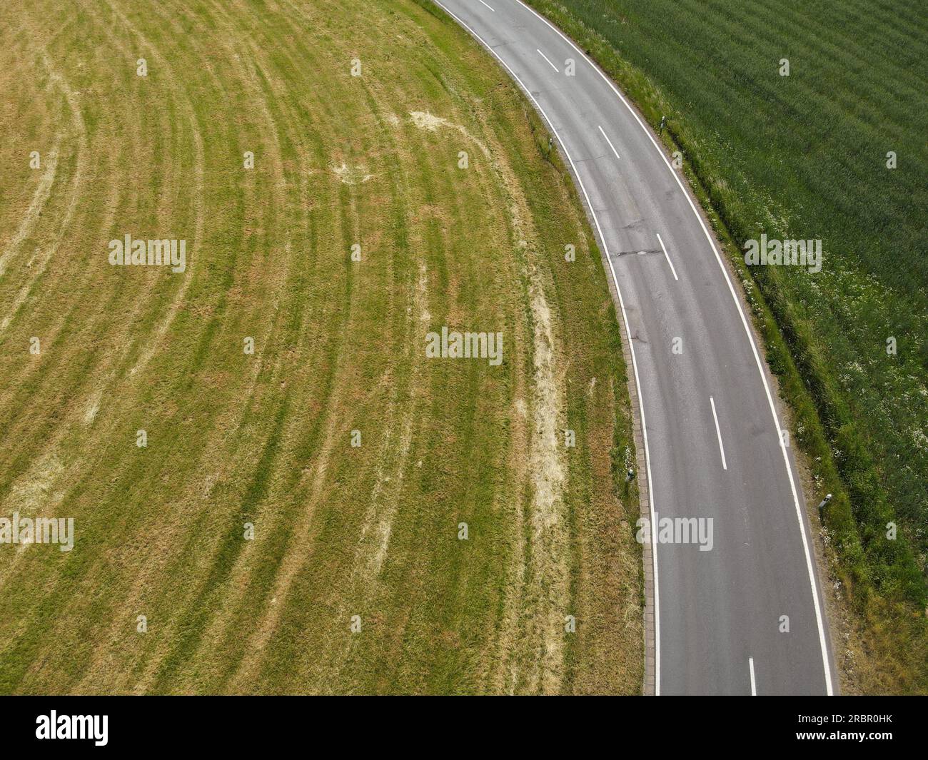 Drone view of a curved asphalt road with white stripes between grass ...