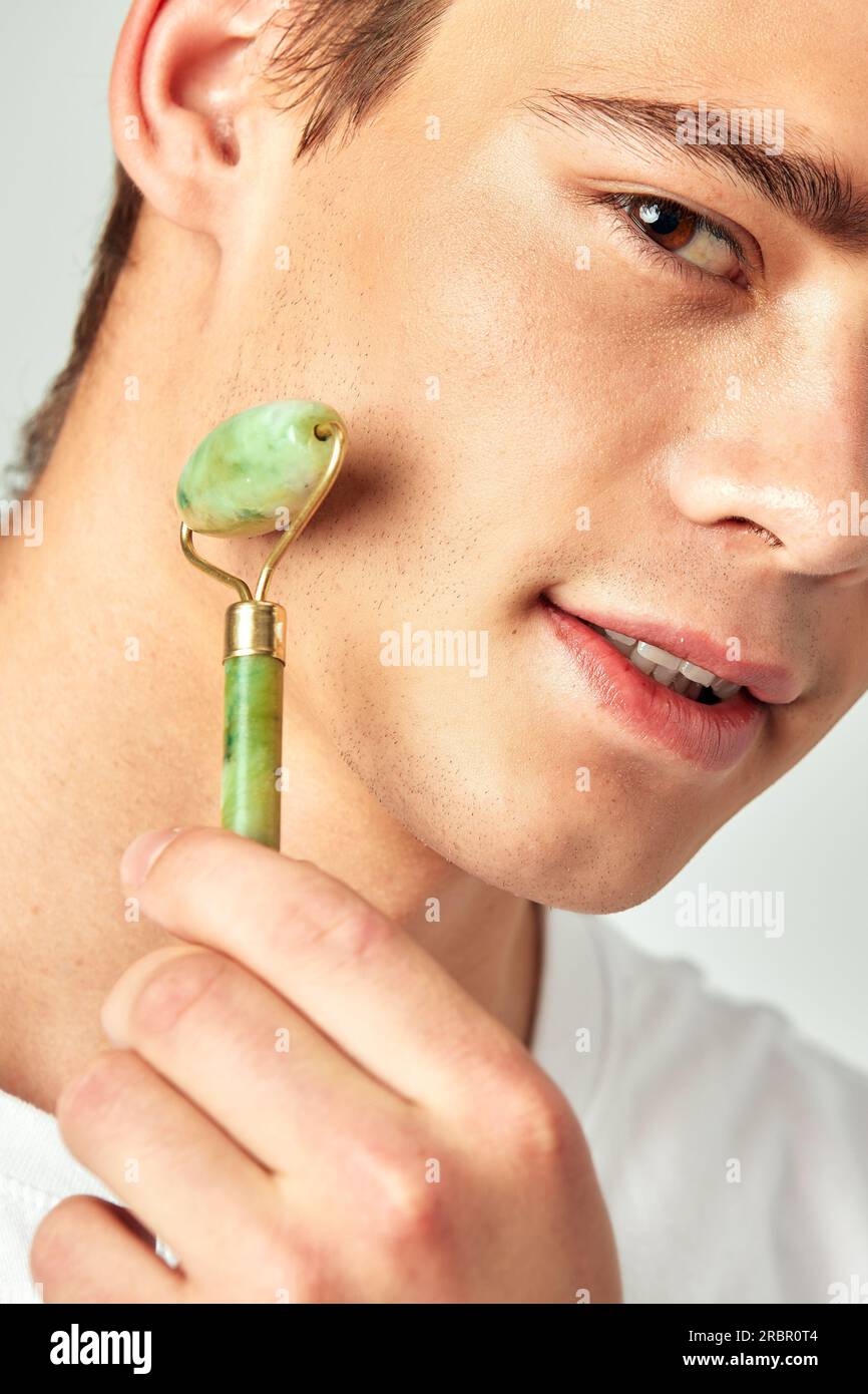 Young handsome smiling guy with brown hair using de-puffing face roller ...