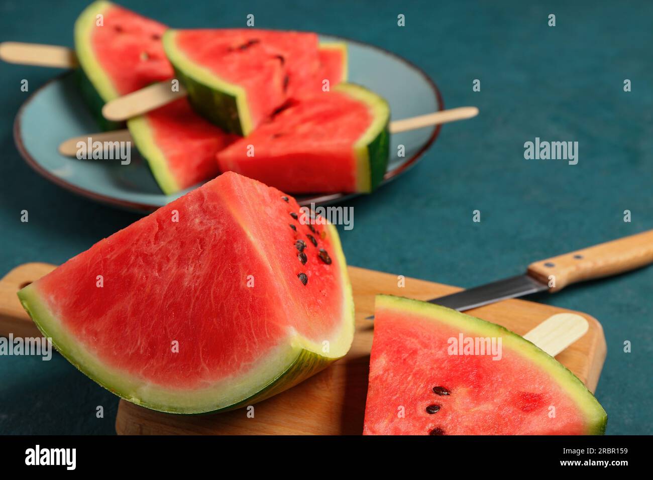 Wooden board and plate with sweet watermelon sticks on green background ...