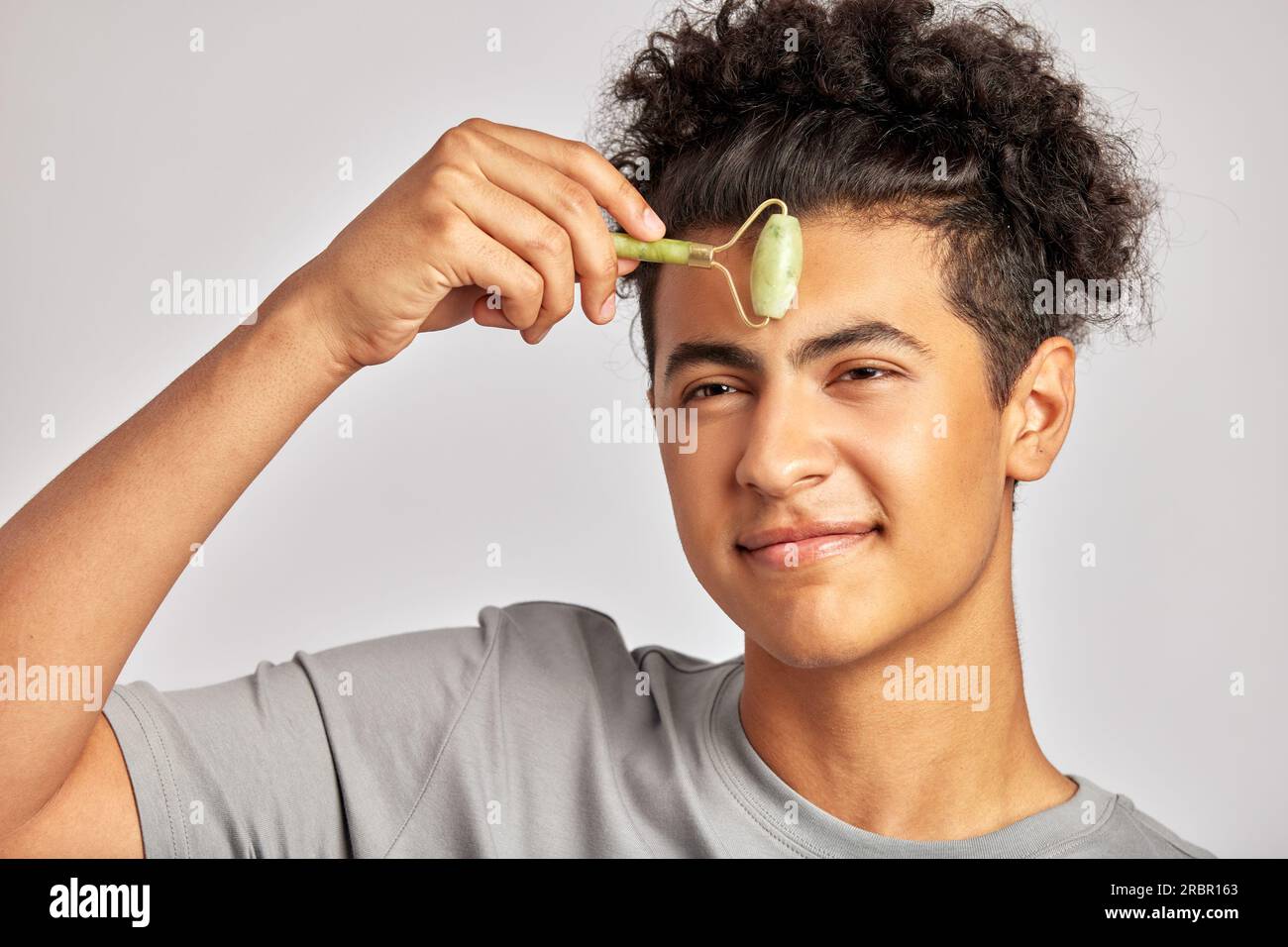 Young handsome smiling guy using jade de-puffing face roller to keep ...