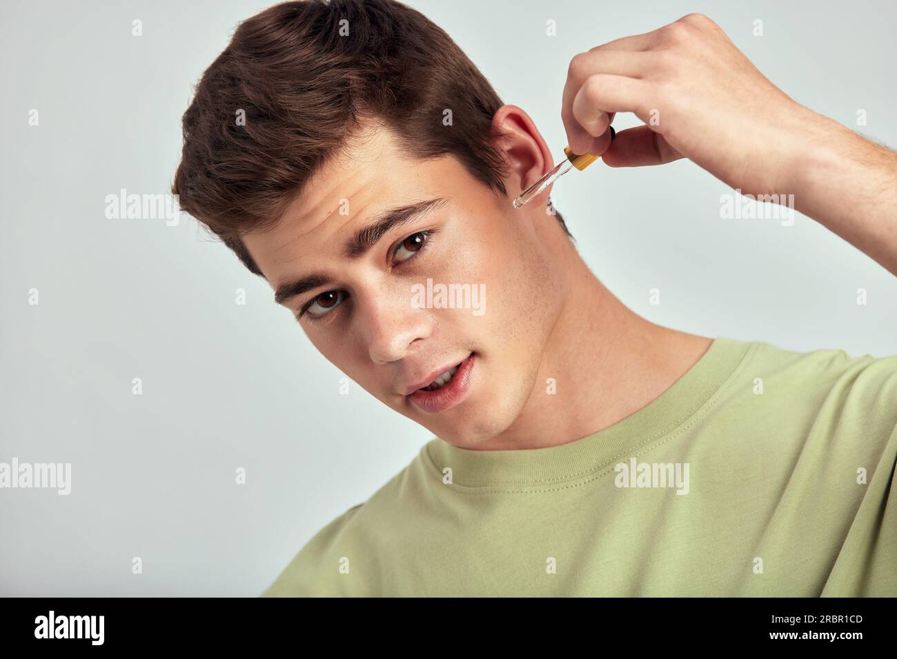 Young handsome smiling guy with brown hair applies beauty serum to his ...