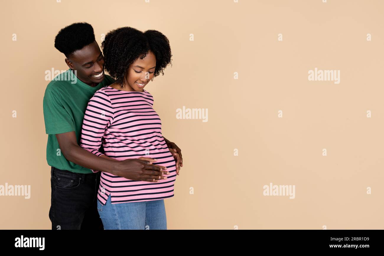 Happy millennial african american husband hugging lady with big belly ...