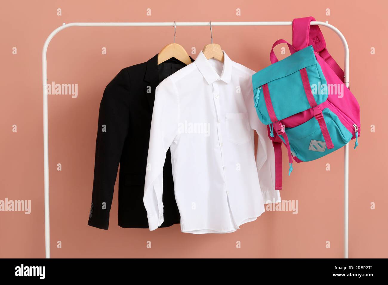 Rack with stylish school uniform and backpack near beige wall in room ...