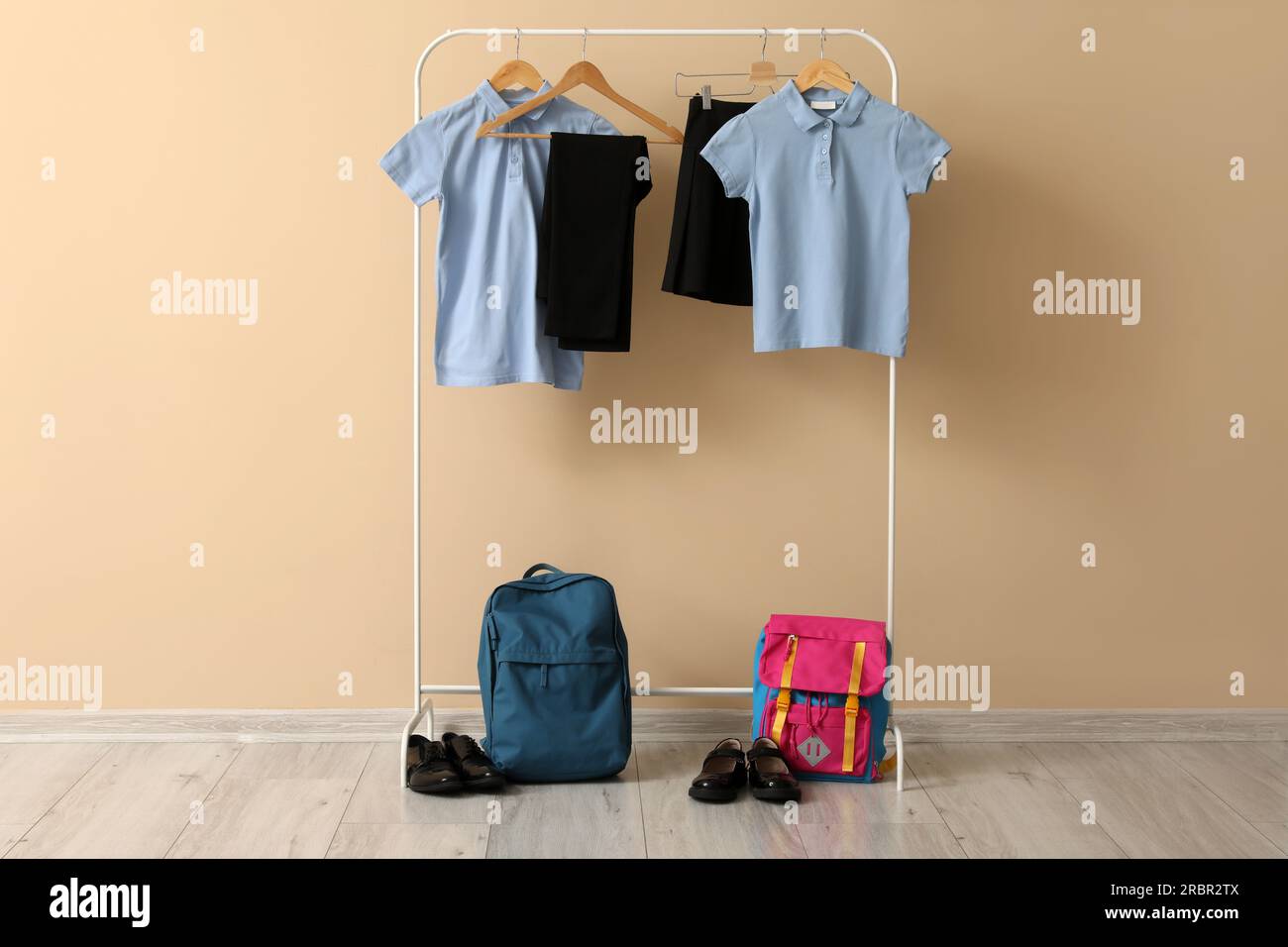 Rack with stylish school uniform, backpacks and shoes near color wall ...
