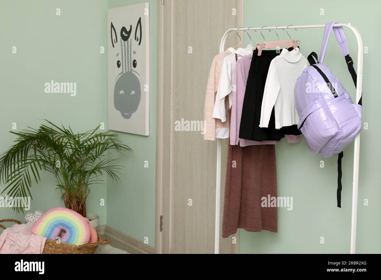 Stylish school uniform and backpack hanging on rack in children's room ...