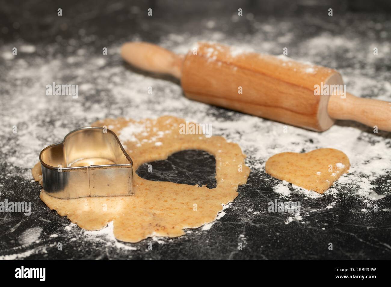 Cookie dough lies unrolled on a dark countertop. Flour is next to it ...