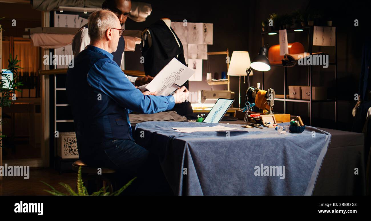 Old couturier teaching pupil skills to design luxury clothing items ...