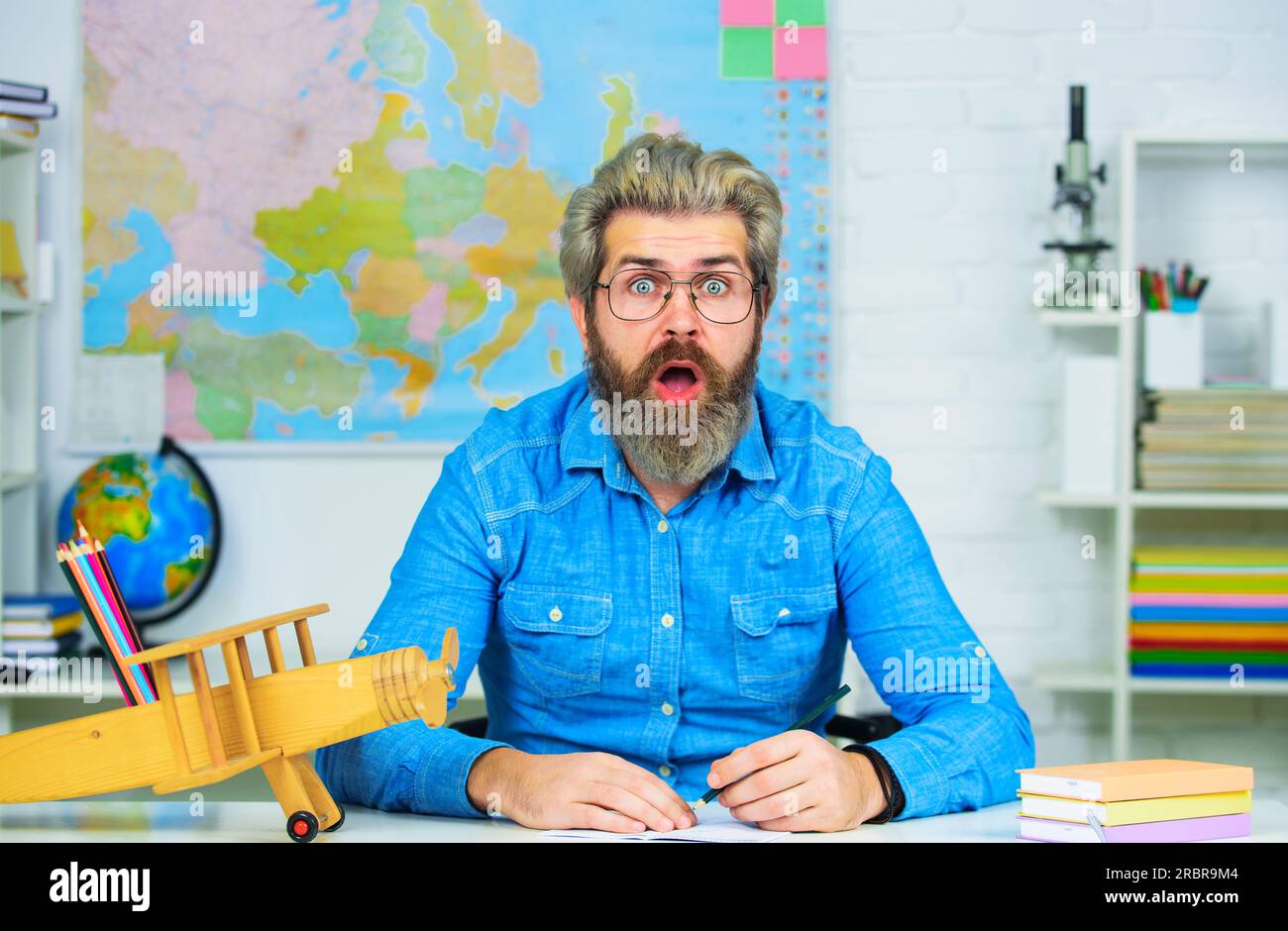 Amazed bearded teacher at desk in classroom. Student preparing for ...