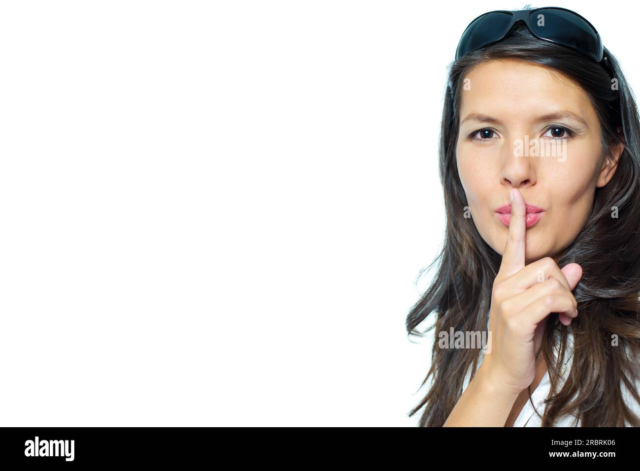 Woman making a shushing gesture raising her finger to her lips as she ...