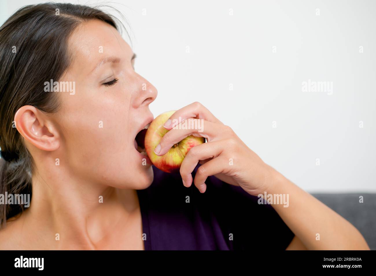 Side view of an attractive young woman biting into a fresh juicy red ...