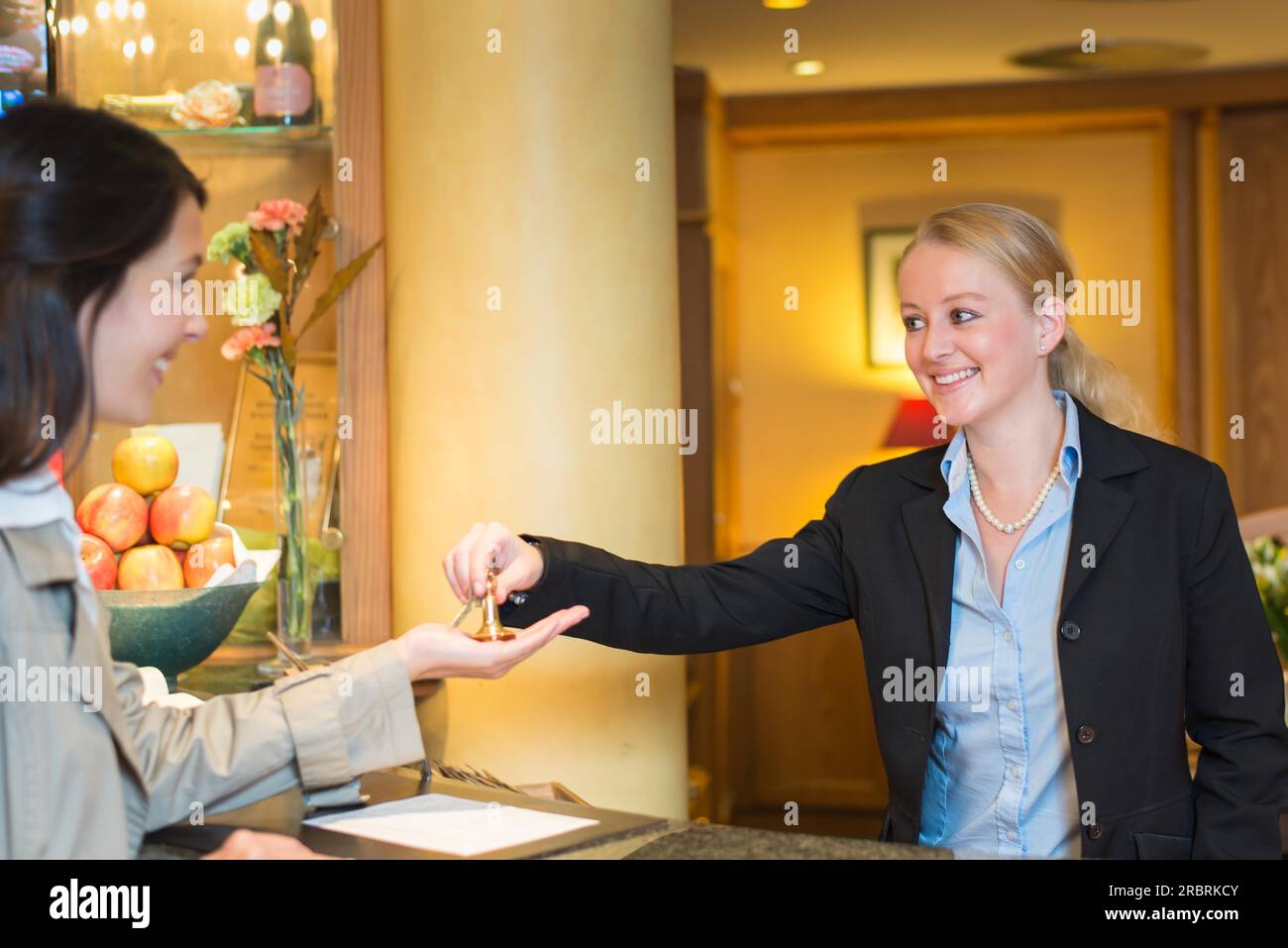 Smiling friendly hotel receptionist standing behind the service desk in ...