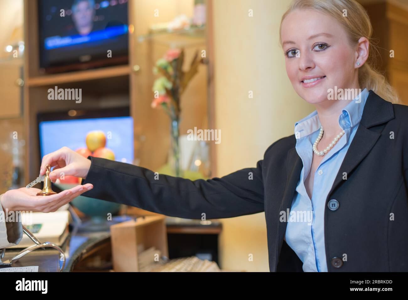 Smiling attractive young female receptionist in a hotel lobby handing ...