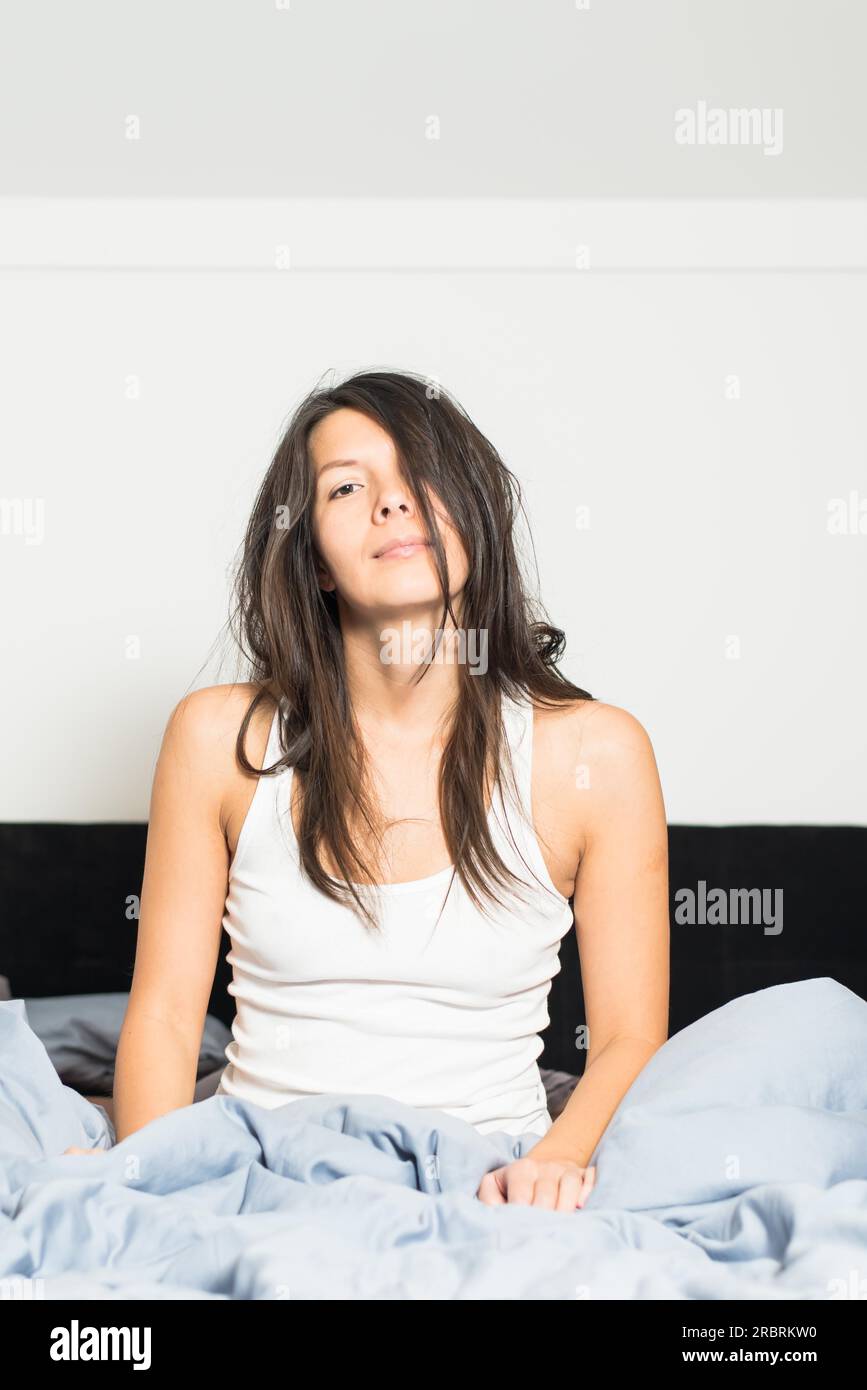 Tired young woman waking up after a nights sleep giving the camera a ...