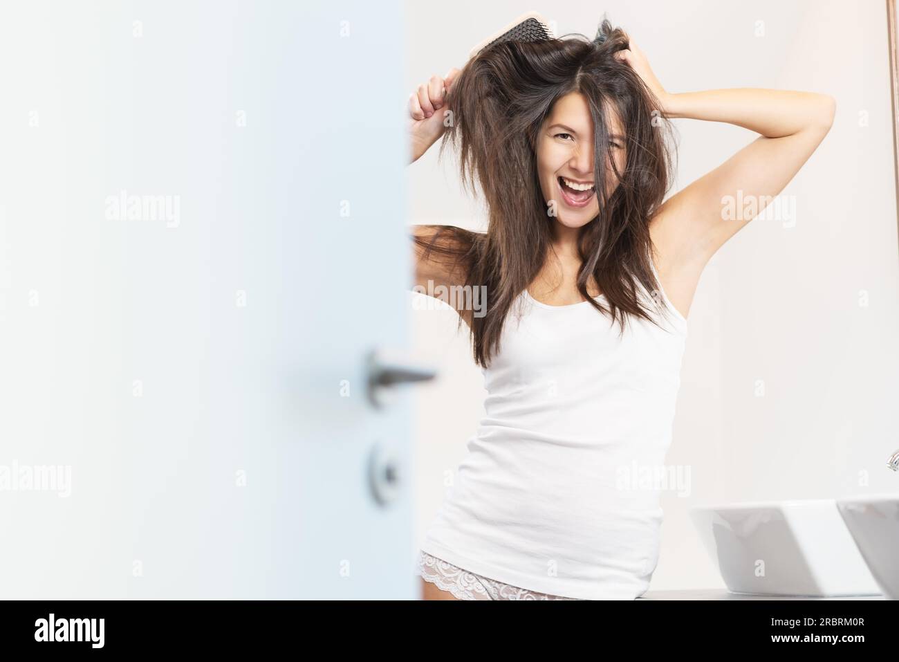 Young woman brushing her tangled long brunette hair in the bathroom in ...