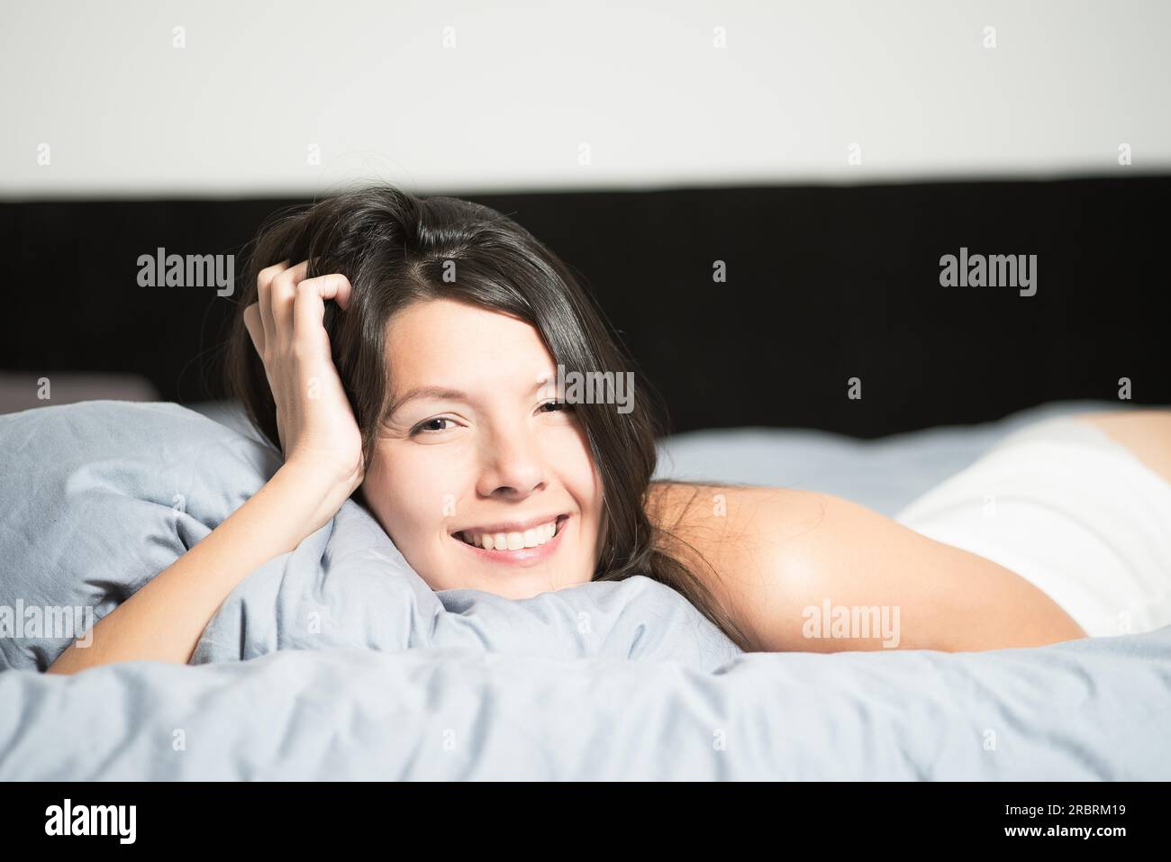 Smiling attractive young woman enjoying a lazy day lying on her stomach ...