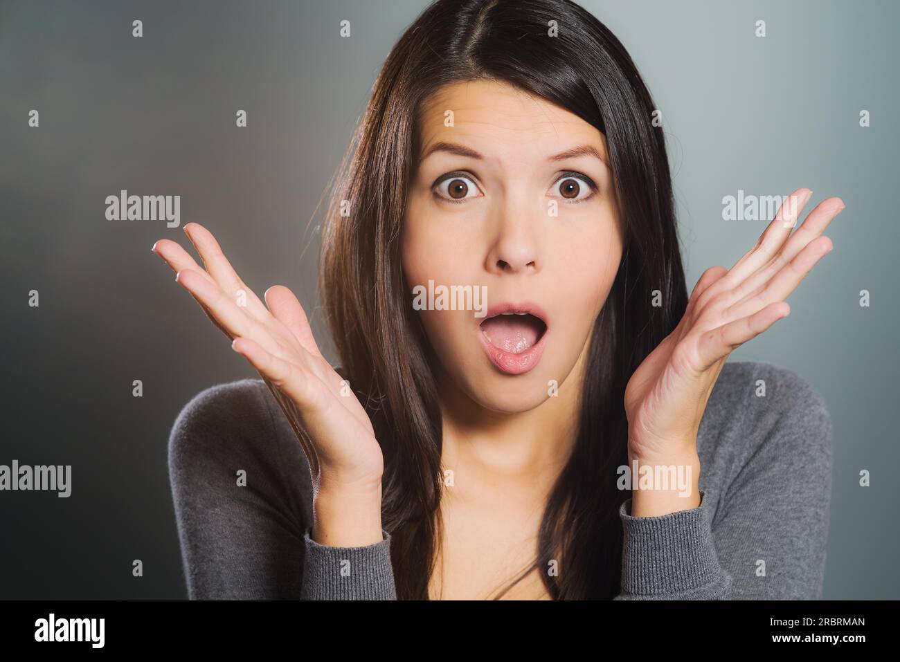 Attractive woman screaming in terror with her hands to her cheeks, mouth open and frightened ...