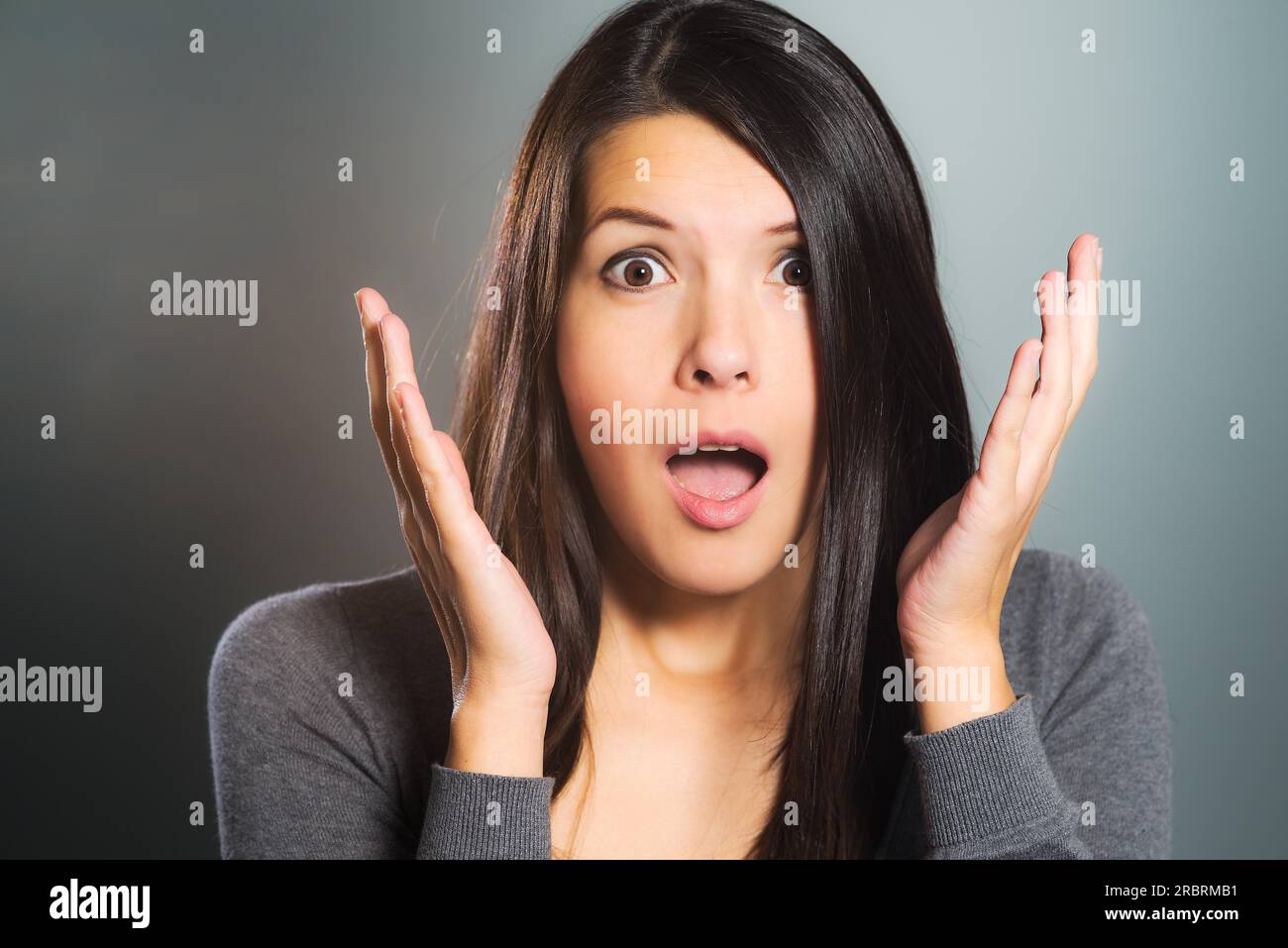 Attractive woman screaming in terror with her hands to her cheeks, mouth open and frightened ...