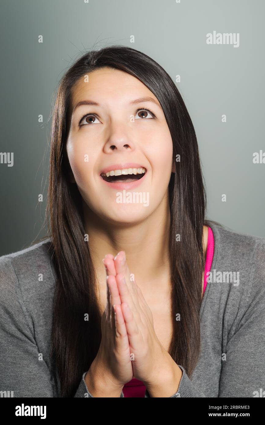 Emotional attractive young woman clasping her hands in supplication or ...