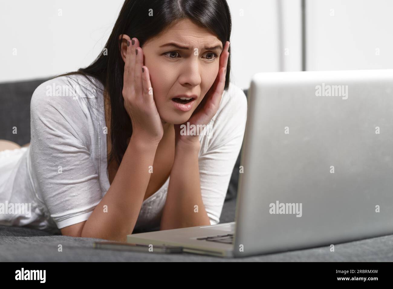 Beautiful young woman looking at her laptop computer with a horrified ...