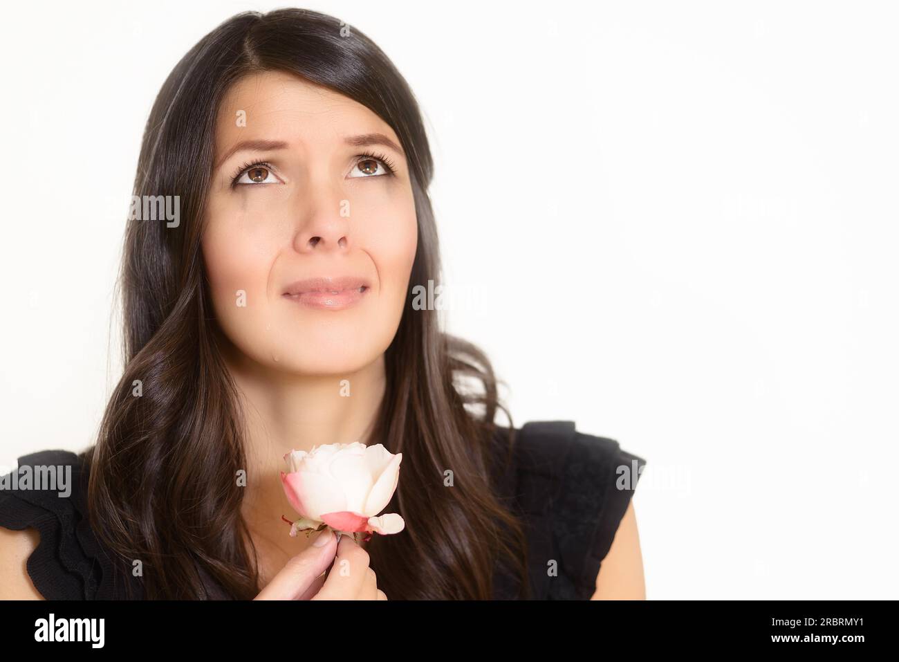 Sorrowful beautiful young woman dressed in black clutching a single ...