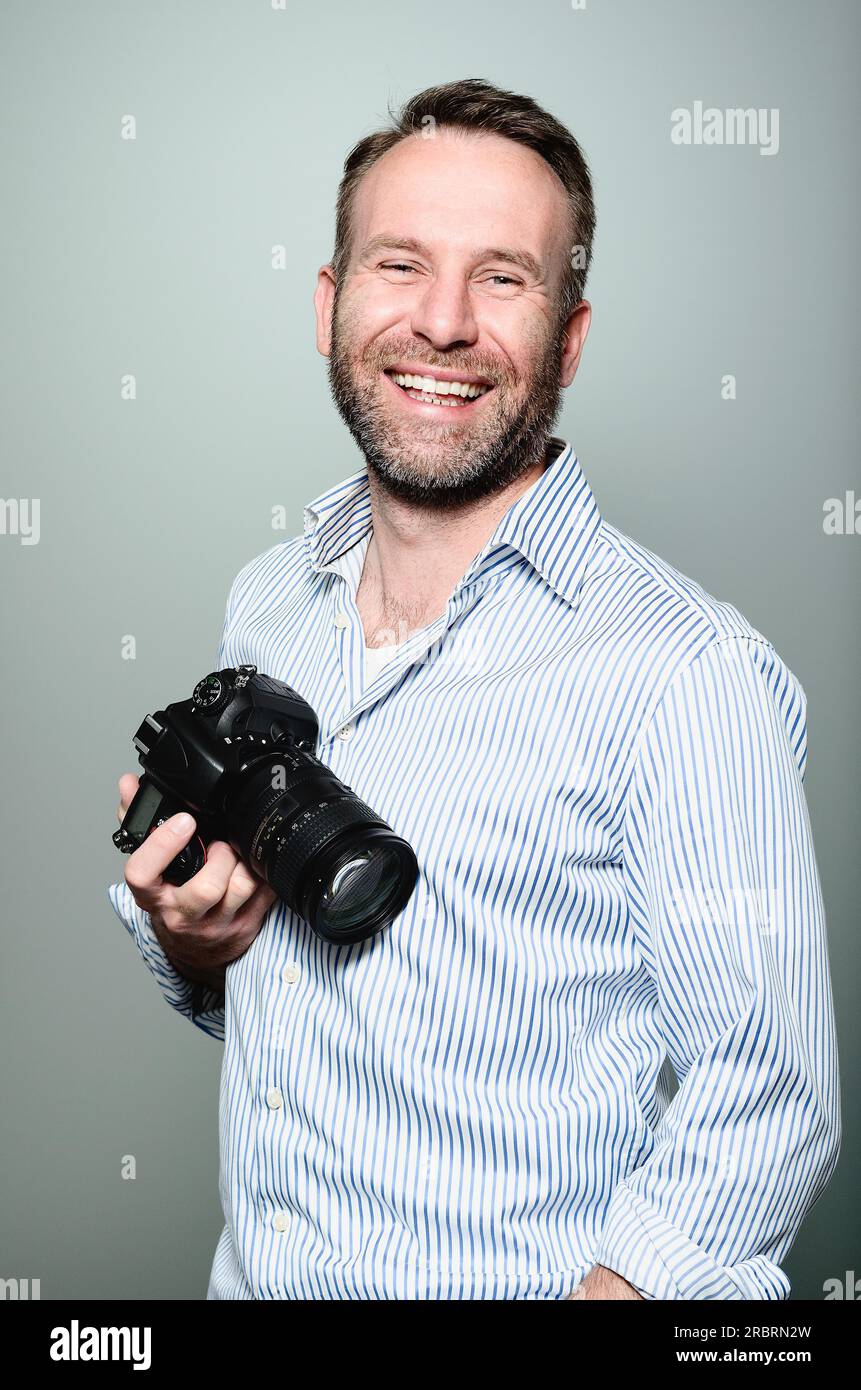 Handsome photographer with a friendly smile standing holding his camera ...