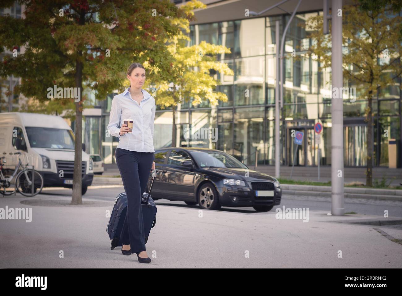 Attractive young woman tourist pulling a trolley down the street on her summer vacation with ...