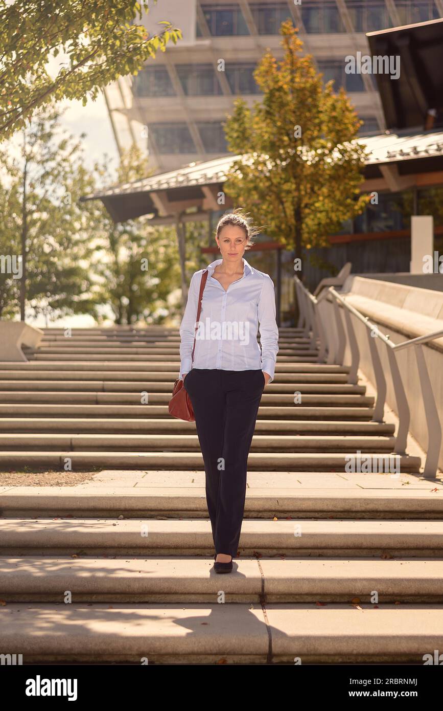 Slender elegant young woman carrying a handbag descending a flight of open-air concrete stairs ...