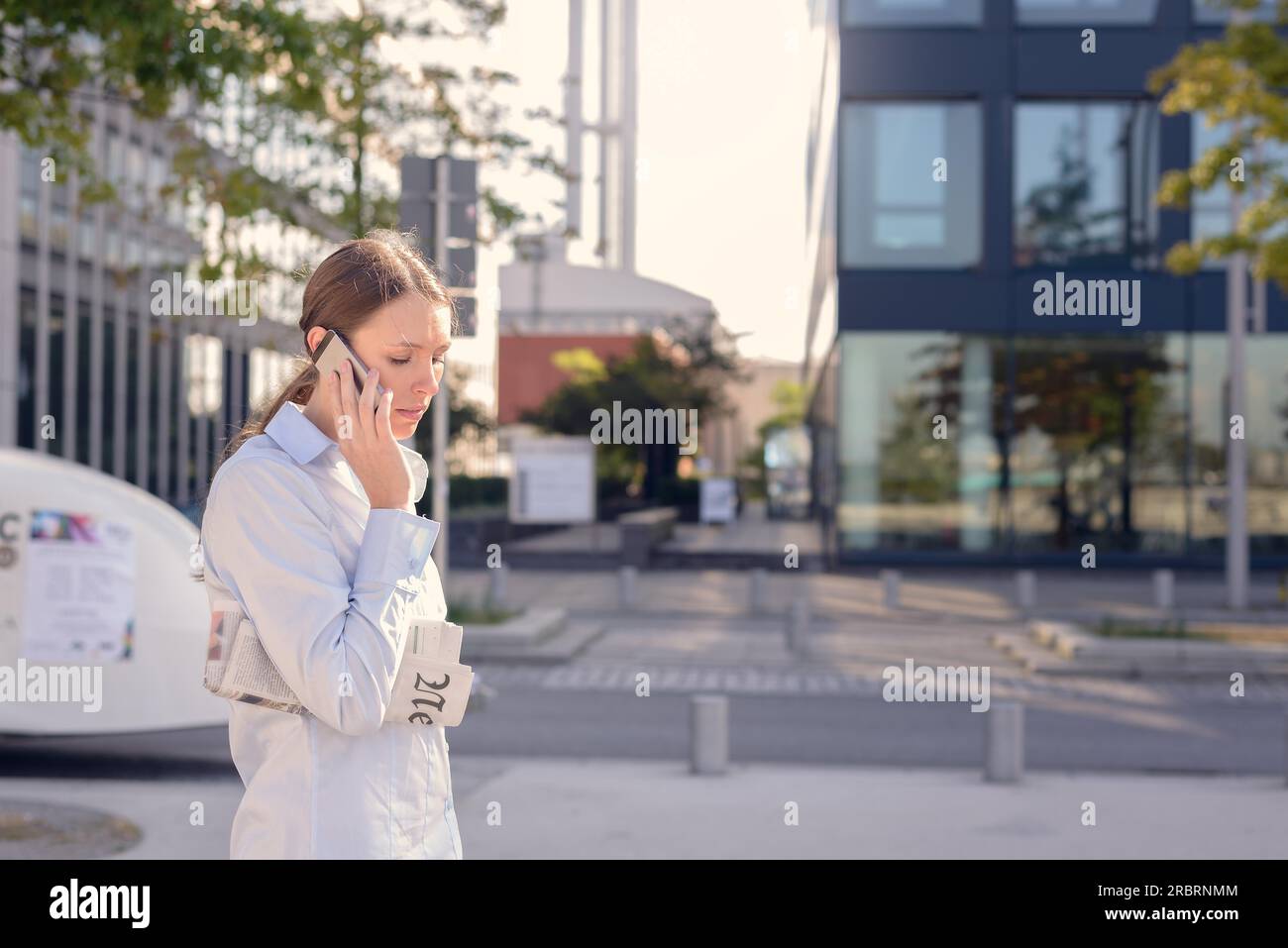 Young woman with a folded newspaper under her arm standing chatting on ...