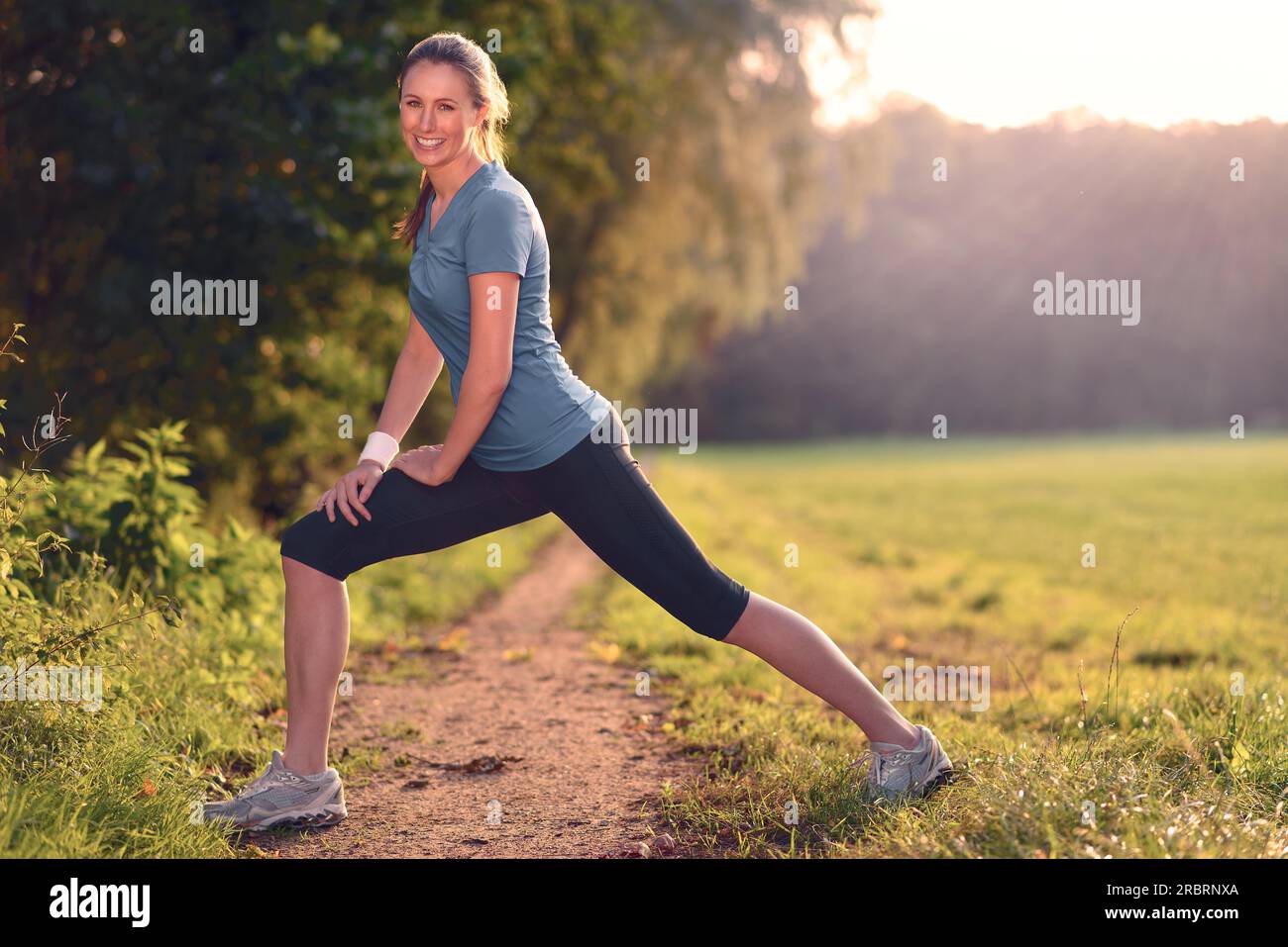 Young woman doing stretching exercises as she limbers up her muscles to ...
