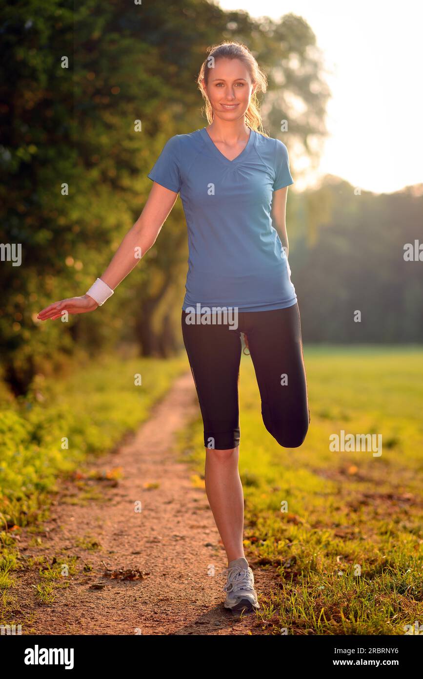 Young woman doing stretching exercises as she limbers up her muscles to ...