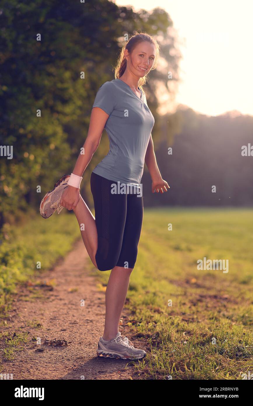Young woman doing stretching exercises as she limbers up her muscles to ...
