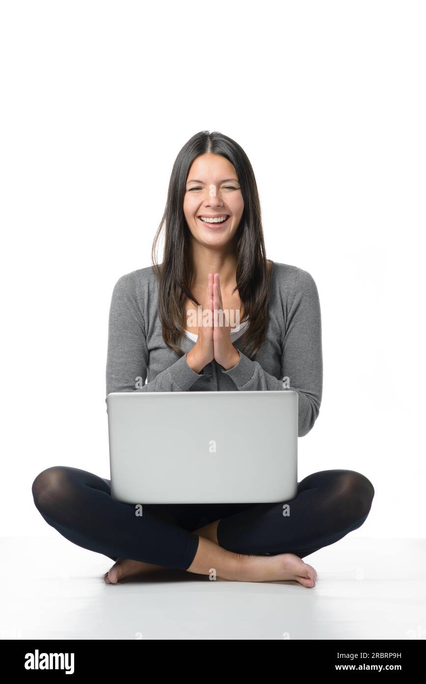Happy young woman meditating with her laptop sitting cross legged and ...