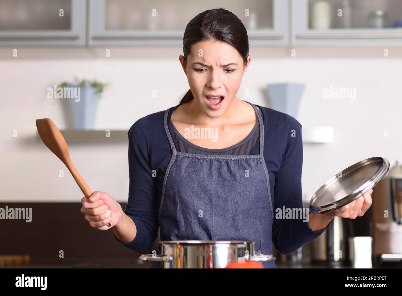 Young housewife having a calamity in the kitchen reacting in shock and ...