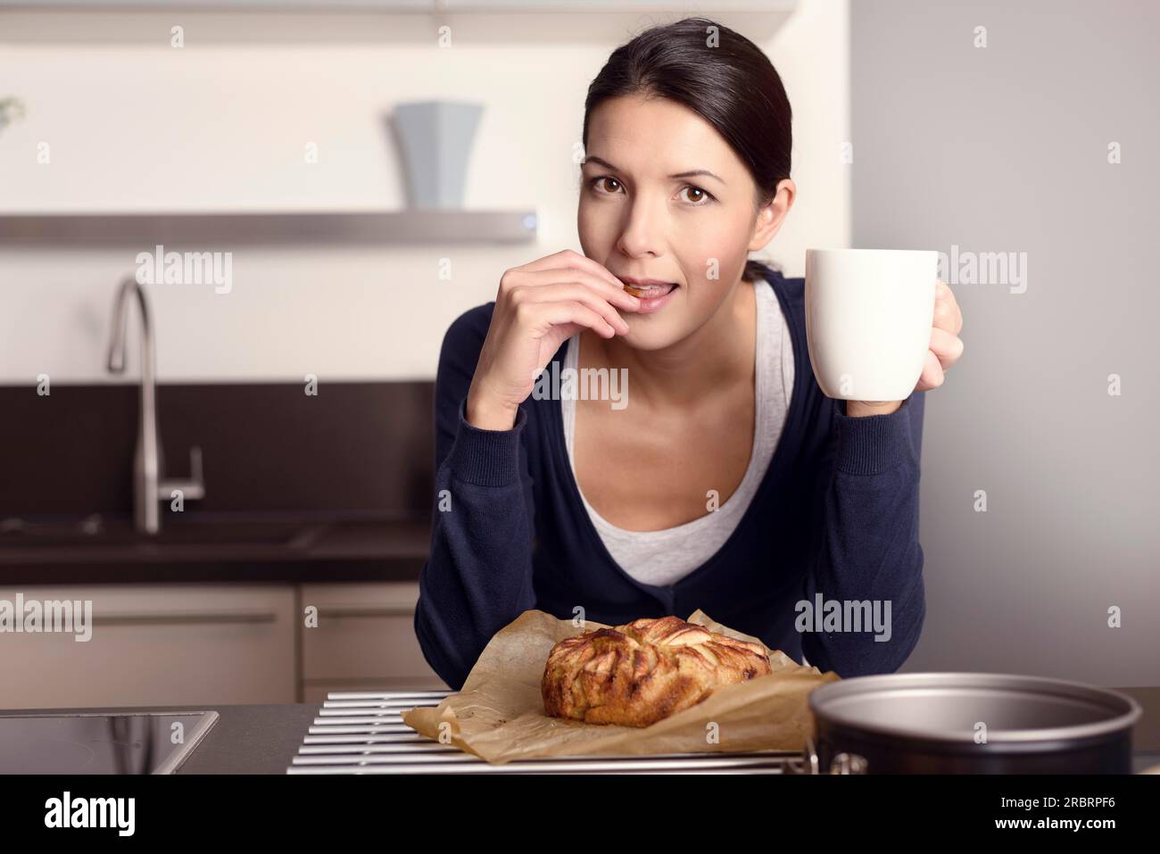 Young woman relaxing in the kitchen with a mug of coffee tasting her ...