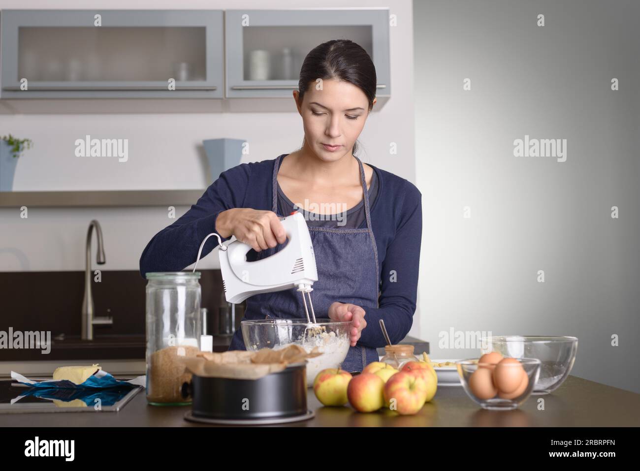 Young woman baking an apple pie in the kitchen standing at the counter ...