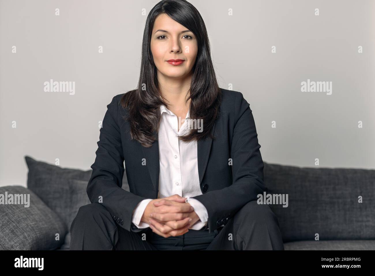 Attractive businesswoman in a slack suit sitting on a sofa looking at ...
