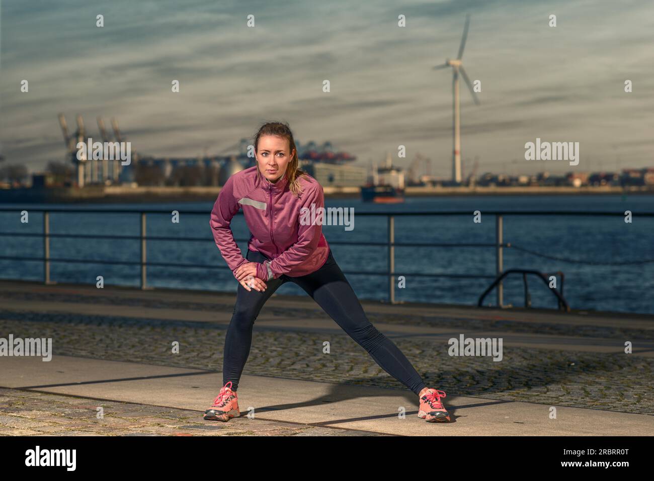 Young woman exercising at the waterfront standing on the esplanade in ...