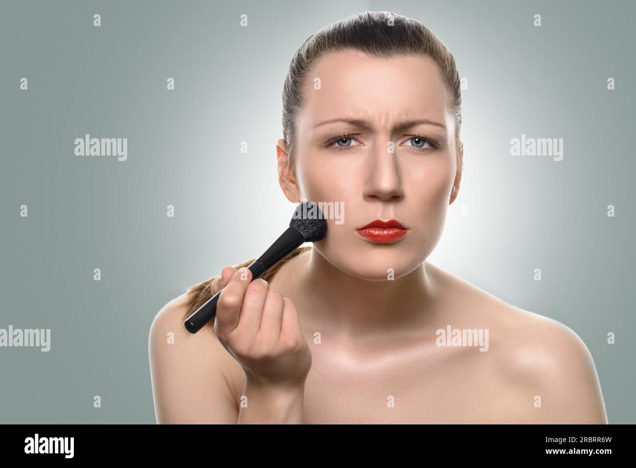 Young woman wearing red lipstick applying blush on her cheeks with a ...